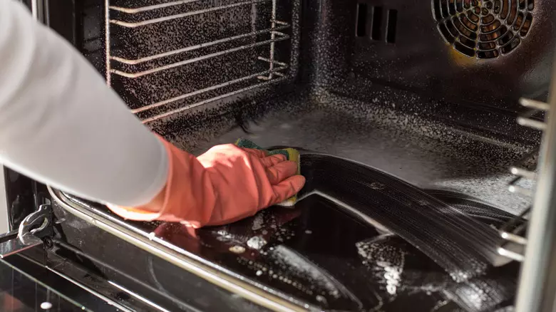 Tangan memakai sarung tangan karet saat membersihkan oven