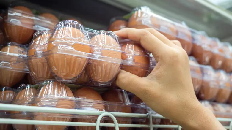 Mano que sostiene el paquete de huevos marrones en el supermercado