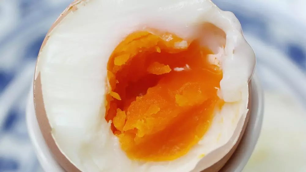 Разбијено кувано јаје у шољи са жутим жуманцем.