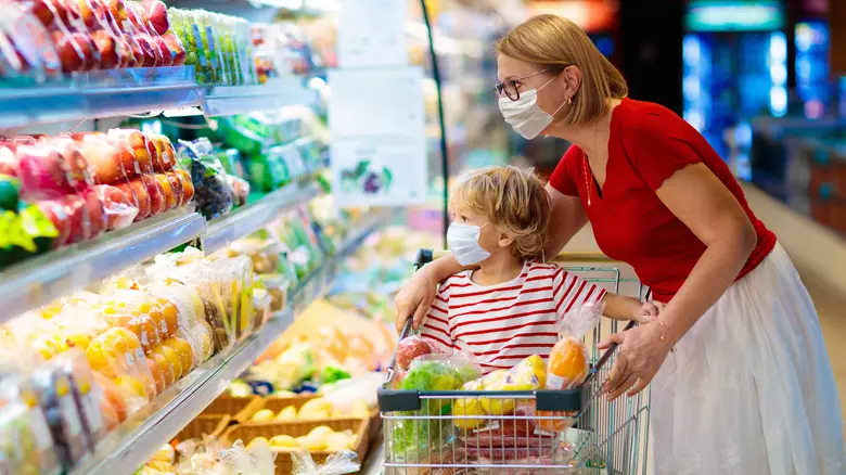 Gemaskerde vrouw en kind boodschappen doen