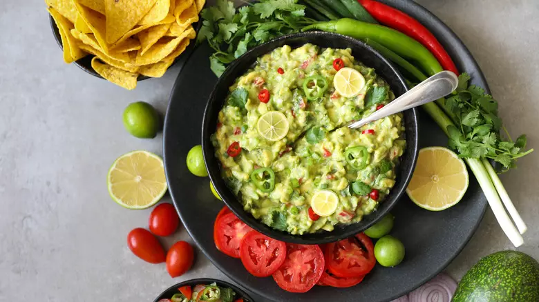 Mísa guacamole vedle rajčat a limetek