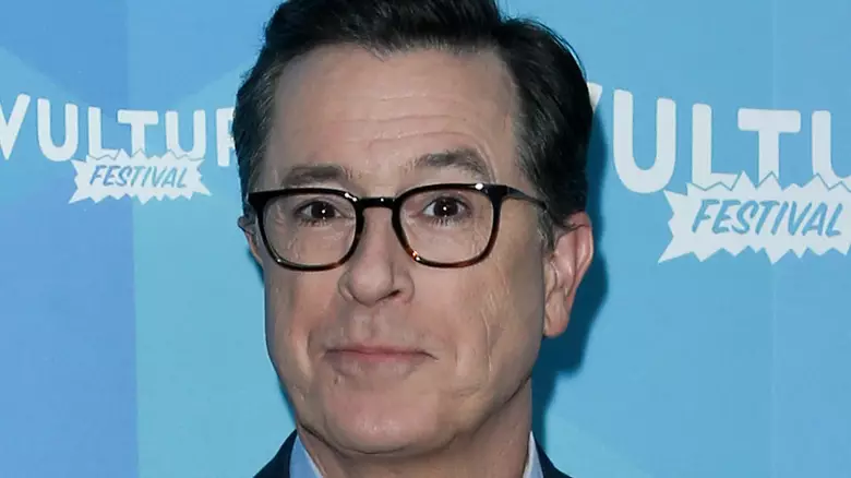 Stephen Colbert wọ awọn gilaasi lori abẹlẹ buluu